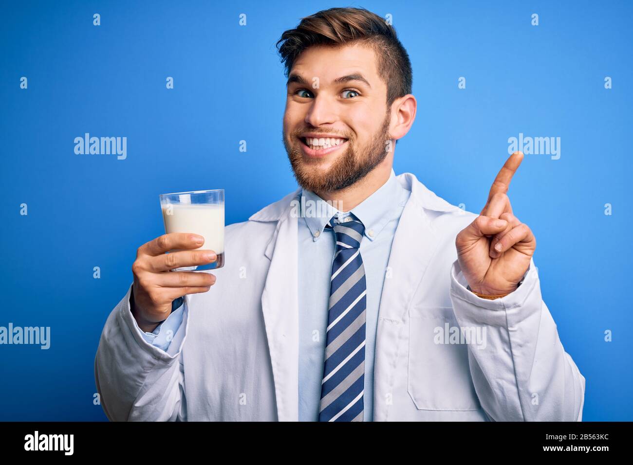 Young blond doctor man with beard and blue eyes wearing coat drinking ...