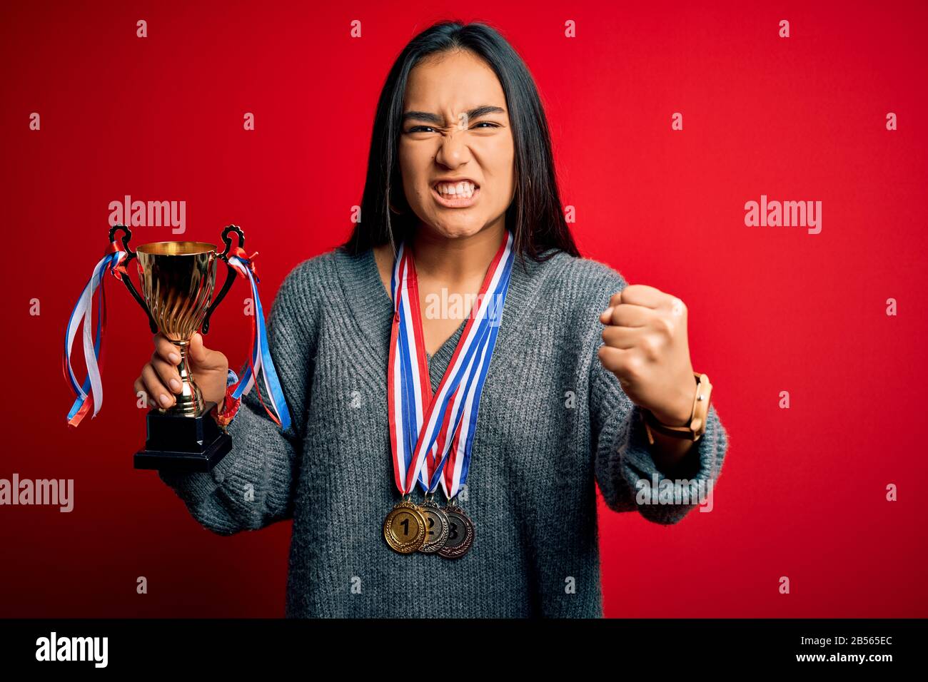 Young beautiful champion asian woman holding trophy wearing medals over ...