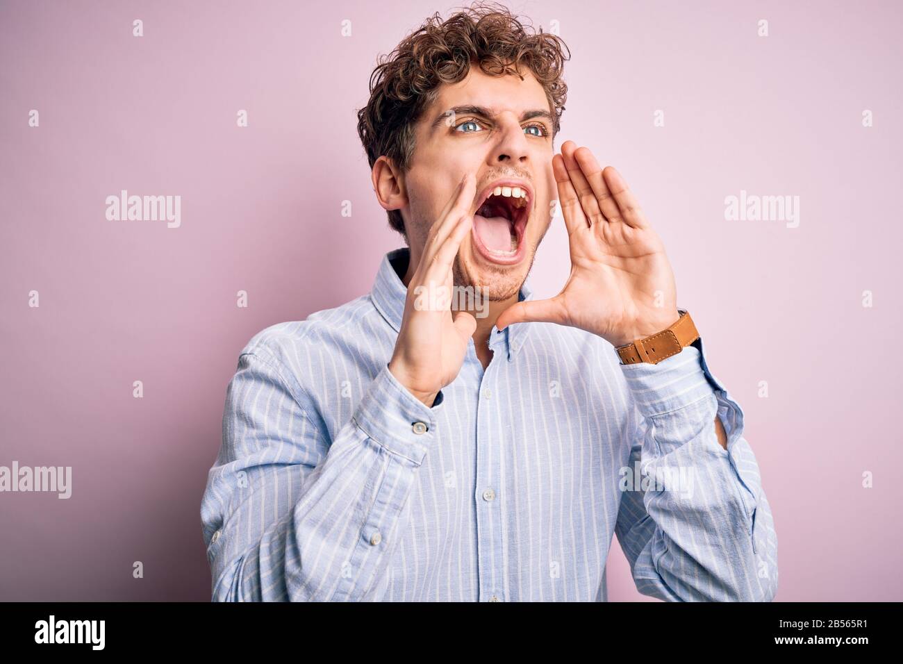 Young blond handsome man with curly hair wearing striped shirt over ...