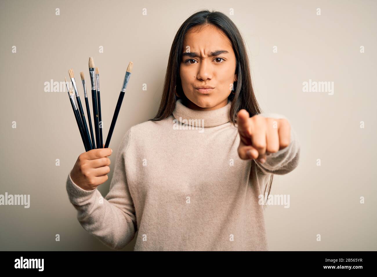 Young beautiful artist asian woman holding paint brushes standing over ...