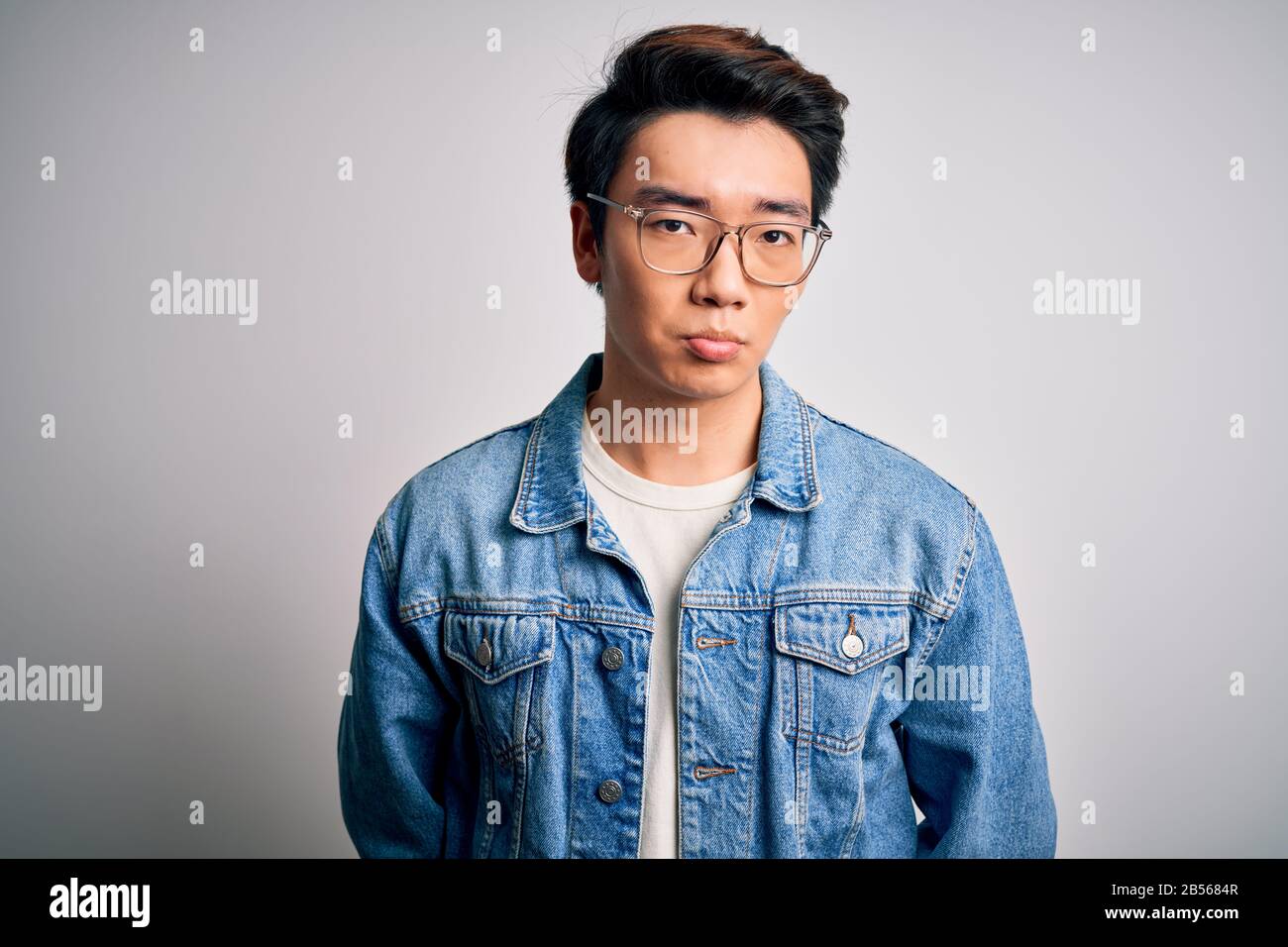Young handsome chinese man wearing denim jacket and glasses over white ...