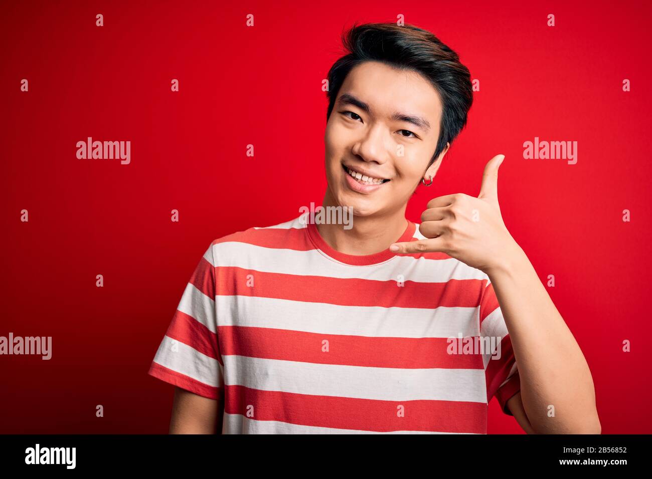 Young handsome chinese man wearing casual striped t-shirt standing over ...