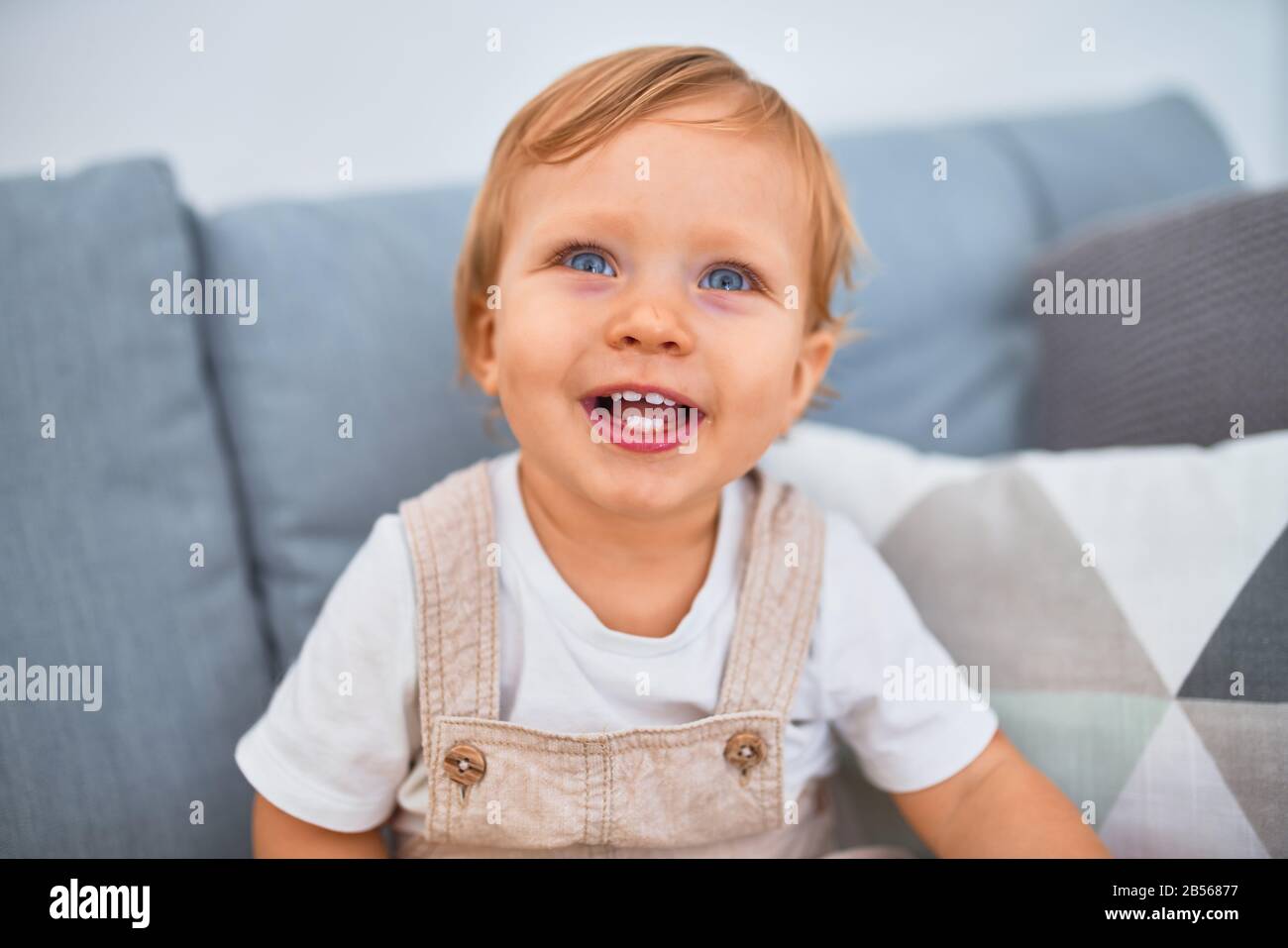 Adorable blonde toddler sitting on the sofa smiling happy at home Stock Photo - Alamy