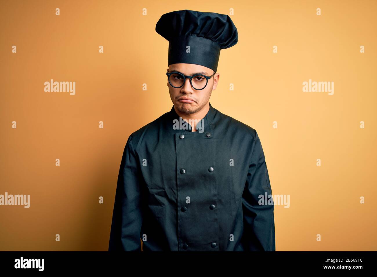 Young brazilian chef man wearing cooker uniform and hat over isolated ...