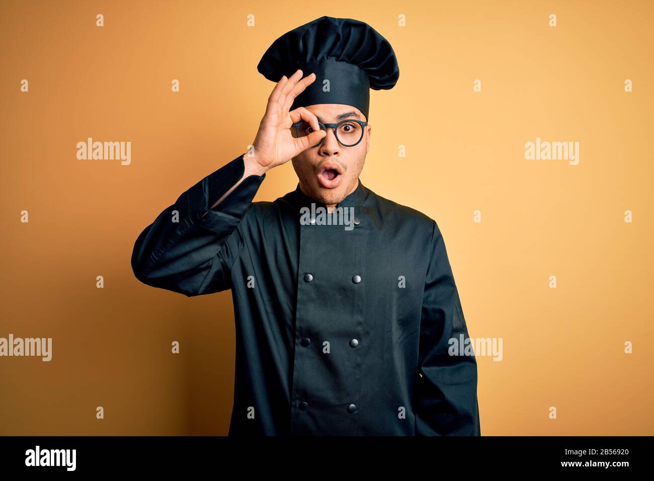 Young brazilian chef man wearing cooker uniform and hat over isolated ...