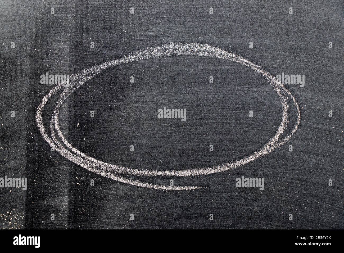 White color chalk hand drawing in circle or oval shape on black board ...