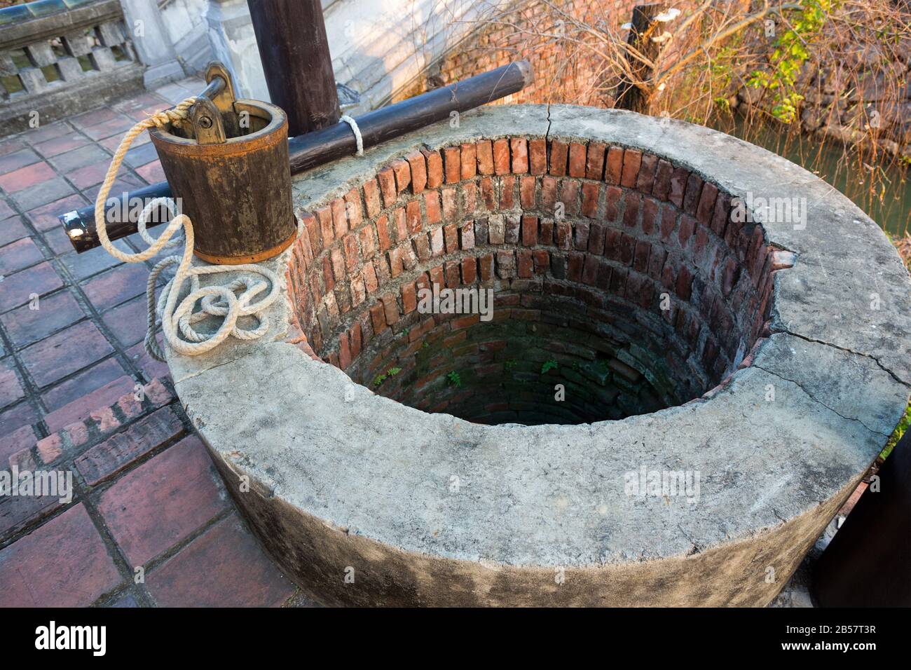 Wooden bucket or barrel tied by rope resting on rim of old brick water ...
