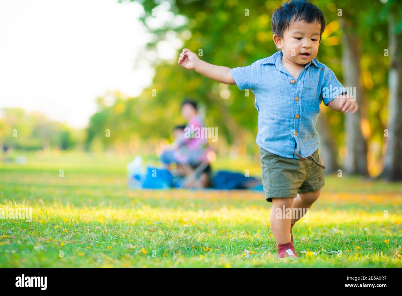 Happy toddler little boy first running on green grass field sunset ...