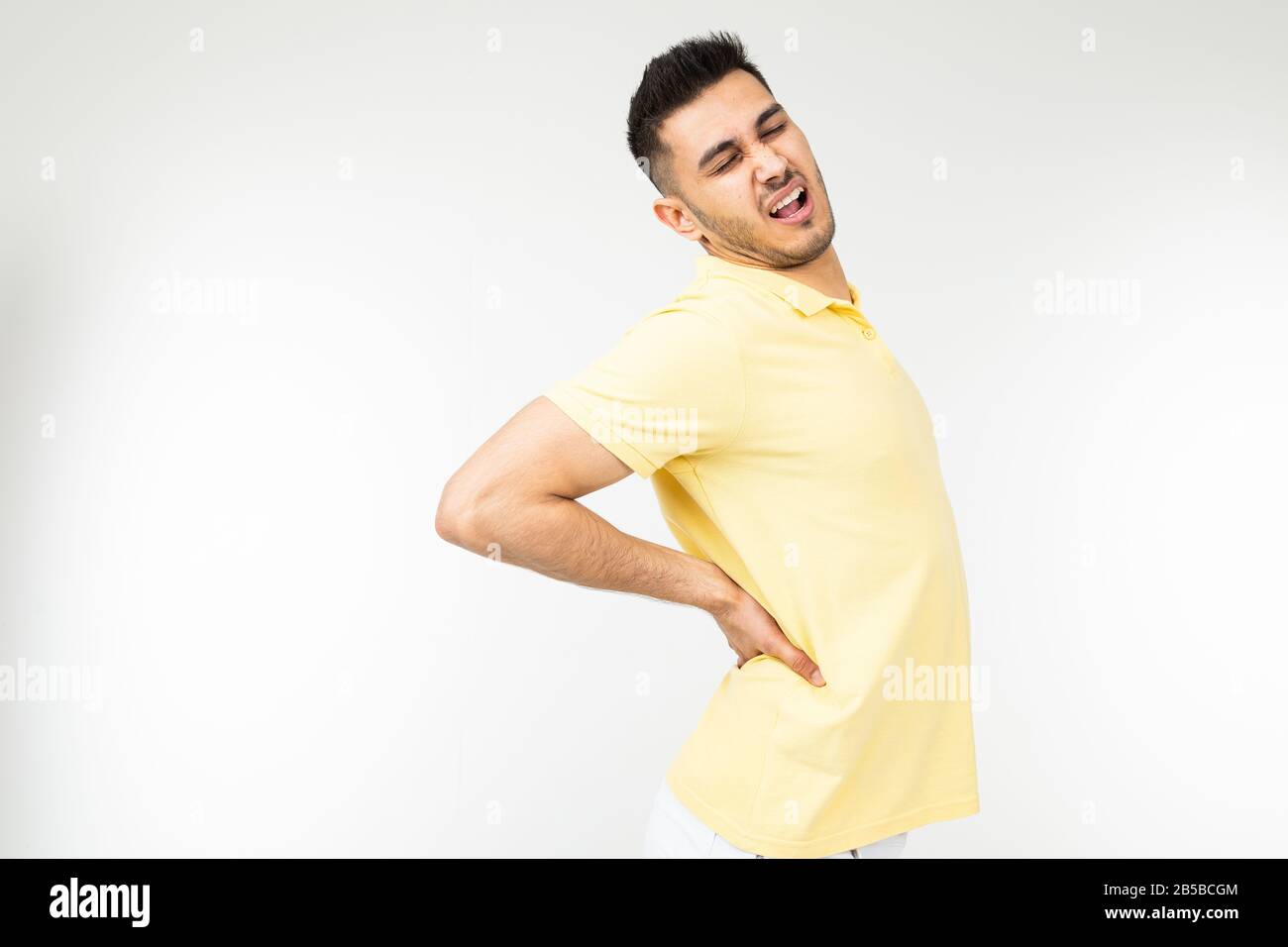 young man feels back pain on a white studio background with copy space ...