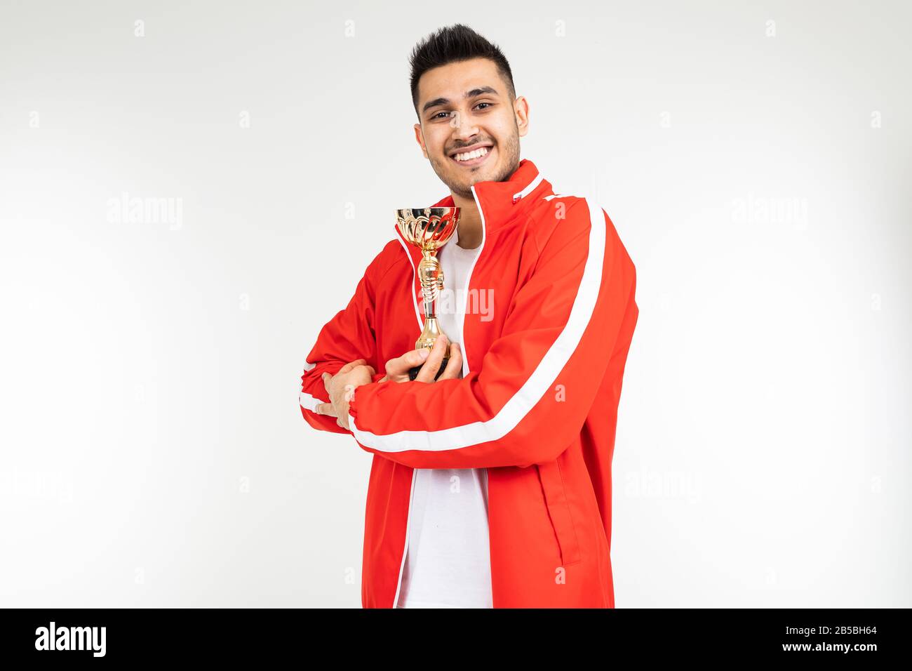 man in a red tracksuit shows off the winner's gold cup on a white ...