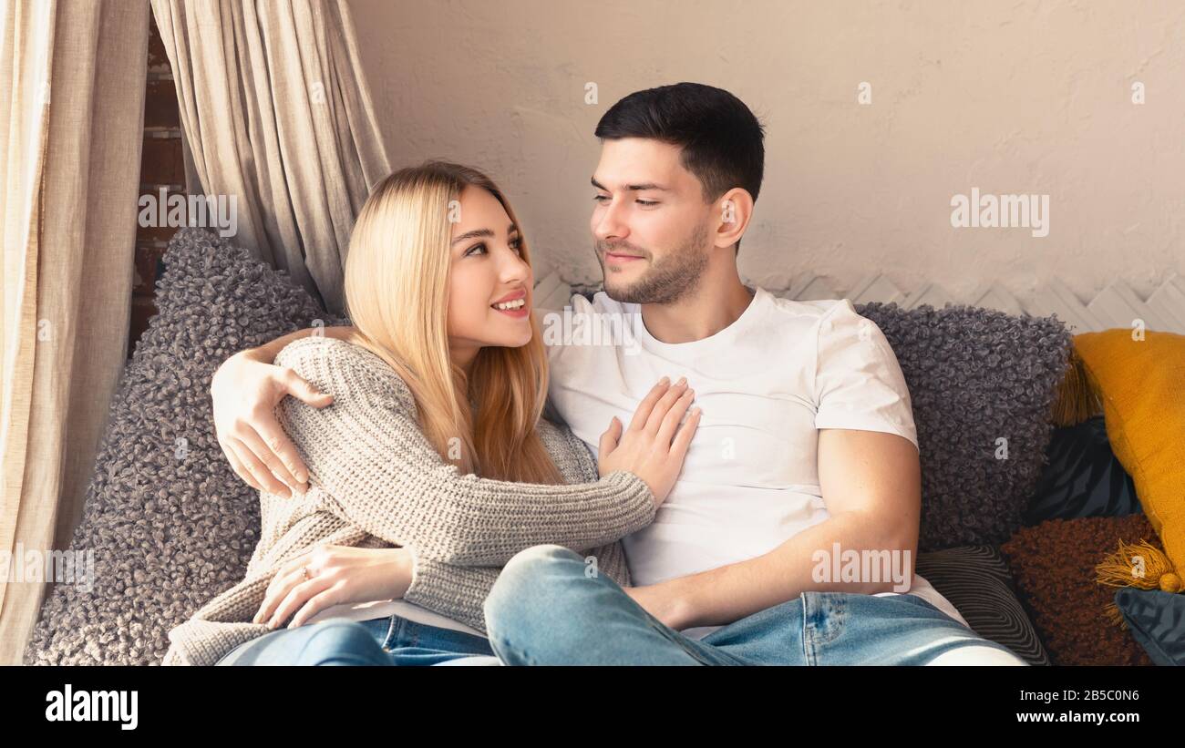 Affectionate boyfriend and girlfriend cuddling on sofa indoors ...