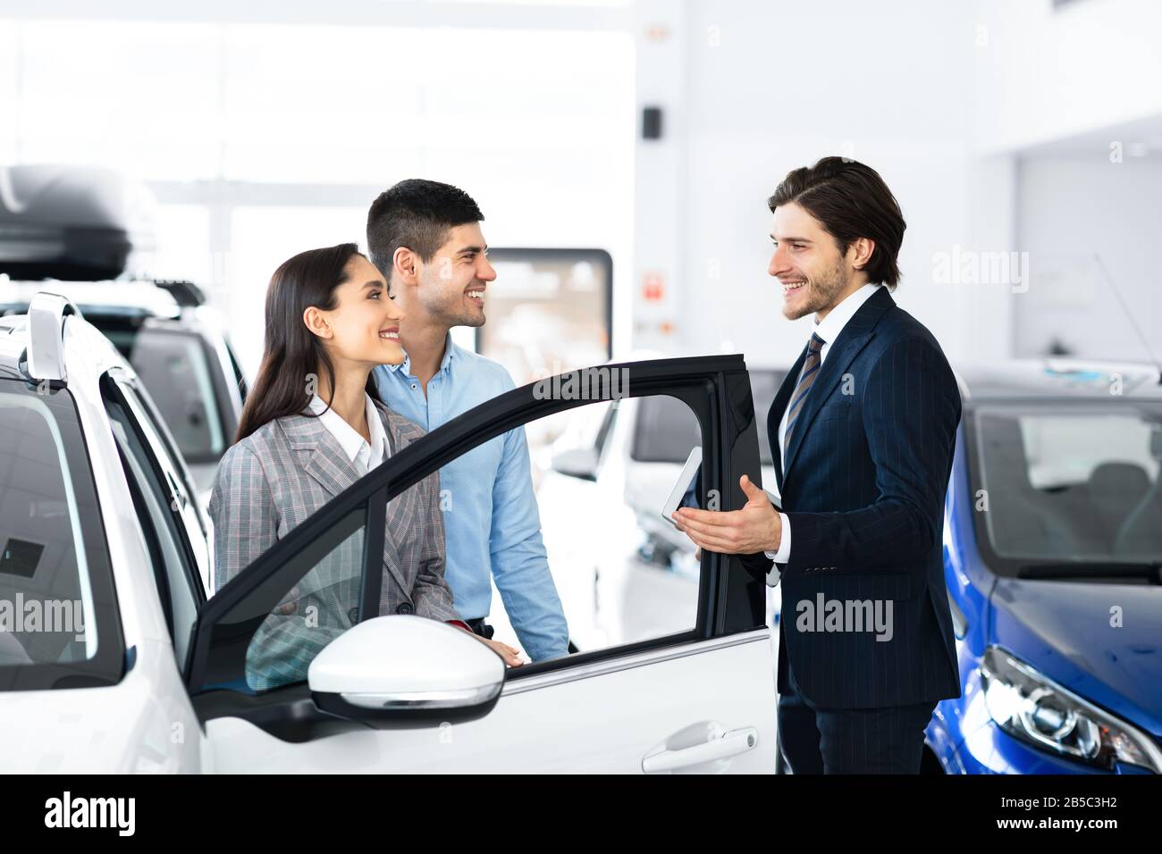 Couple Choosing Automobile With Professional Dealer In Luxury ...