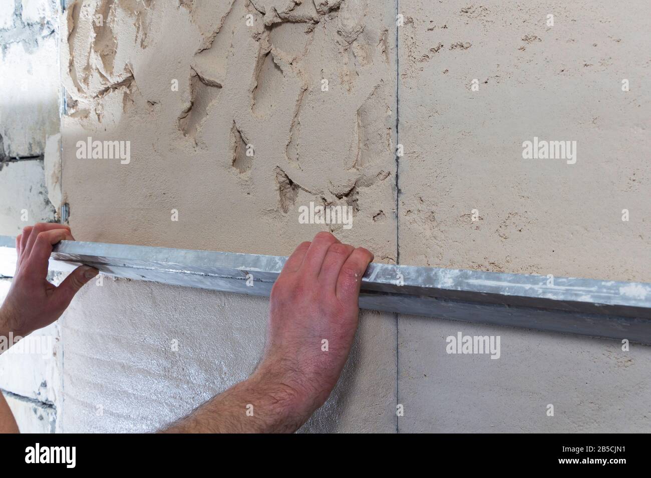 Construction worker with a long spatula to plaster the wall by hand ...