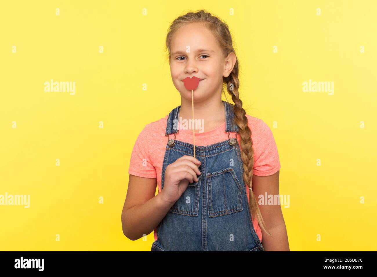 Portrait of charming happy little girl with braid in denim overalls ...