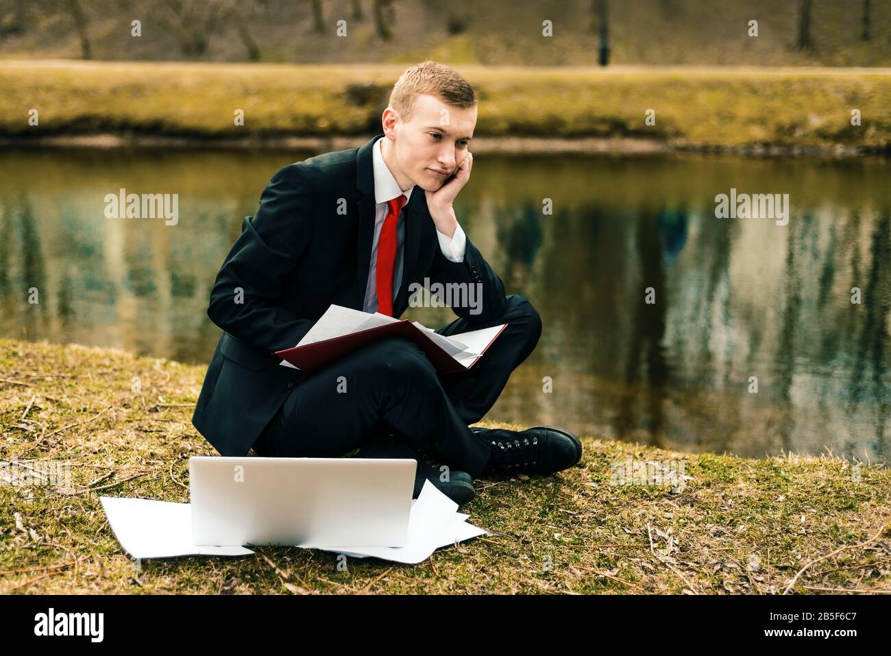 sad young businessman at work in nature by the river. remote work and ...