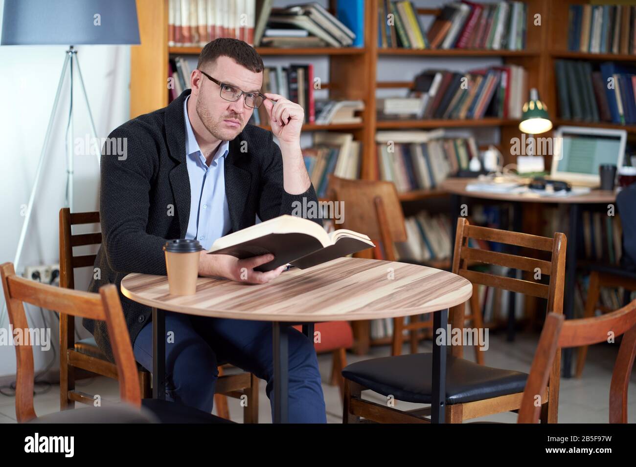 Man reading book and drinking coffee in a library cafe with many books ...