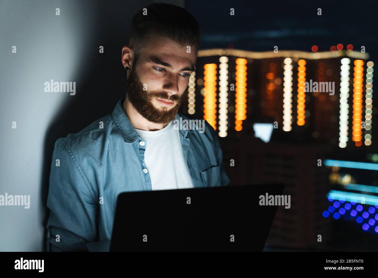 Concentrated young man working on laptop computer while standing ...