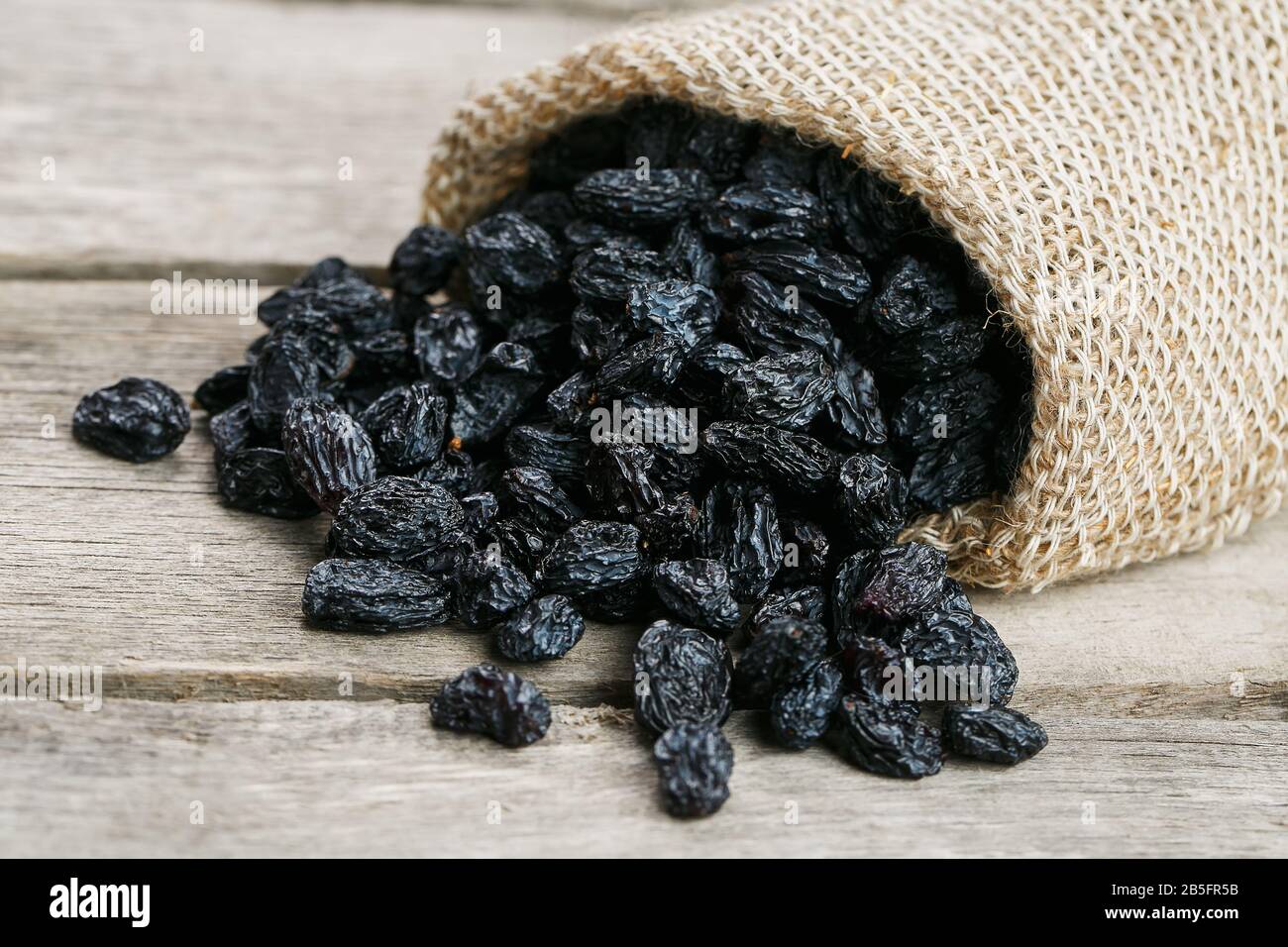 Black raisins in burlap bag over wooden gray table. Raisins are one of ...