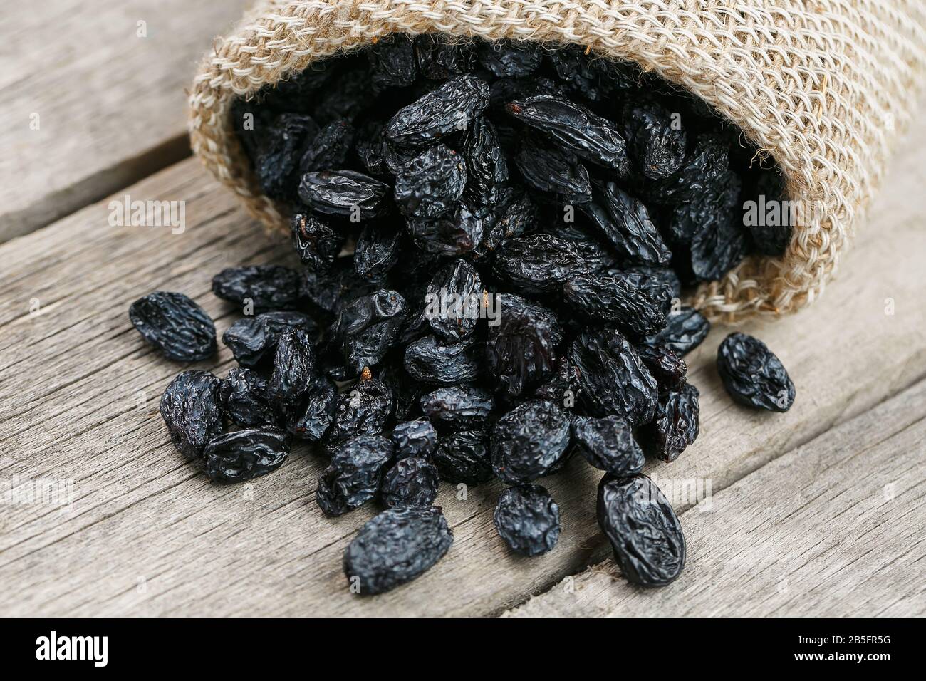 Black raisins in burlap bag over wooden gray table. Raisins are one of ...