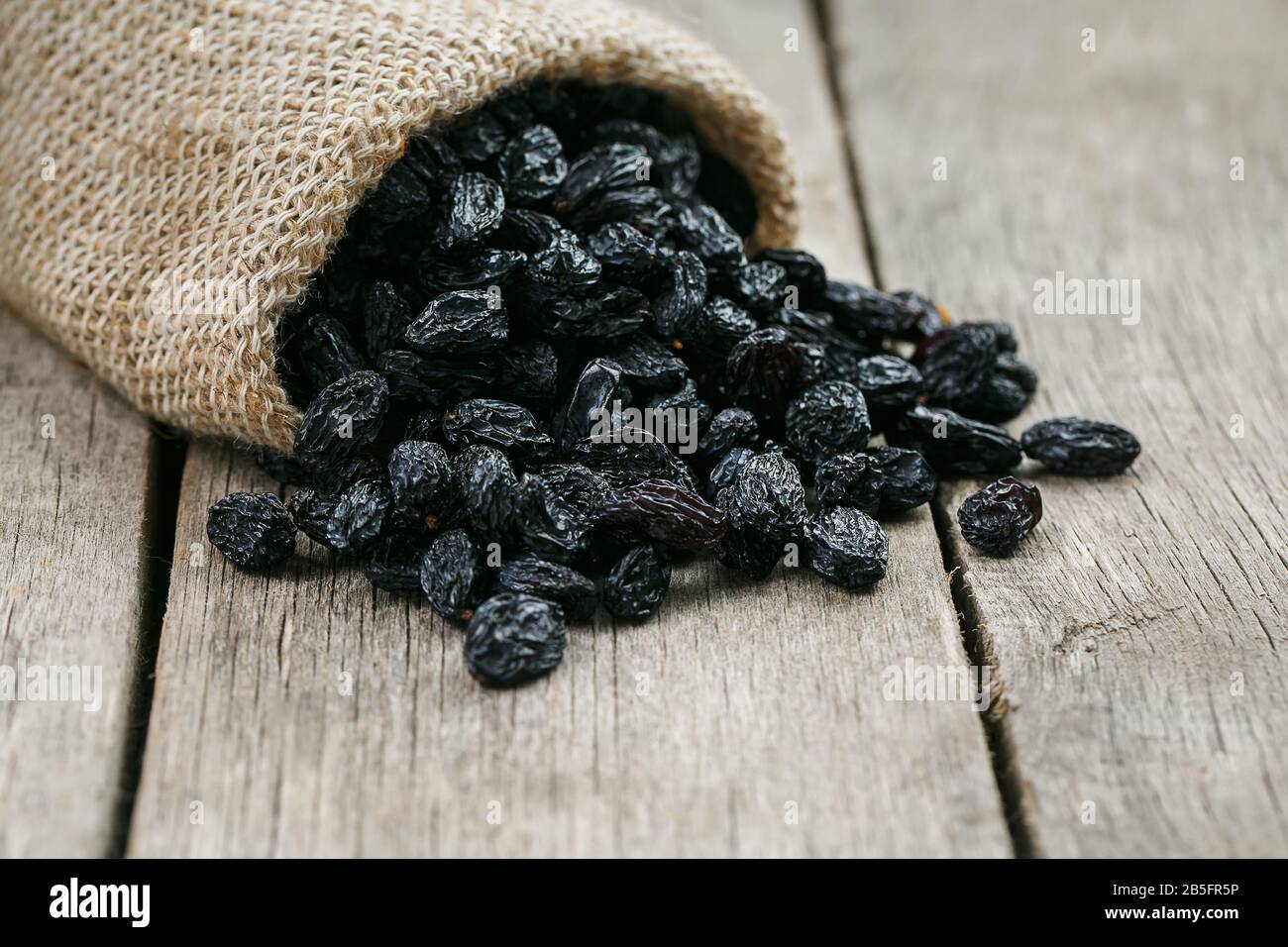 Black raisins in burlap bag over wooden gray table. Raisins are one of ...