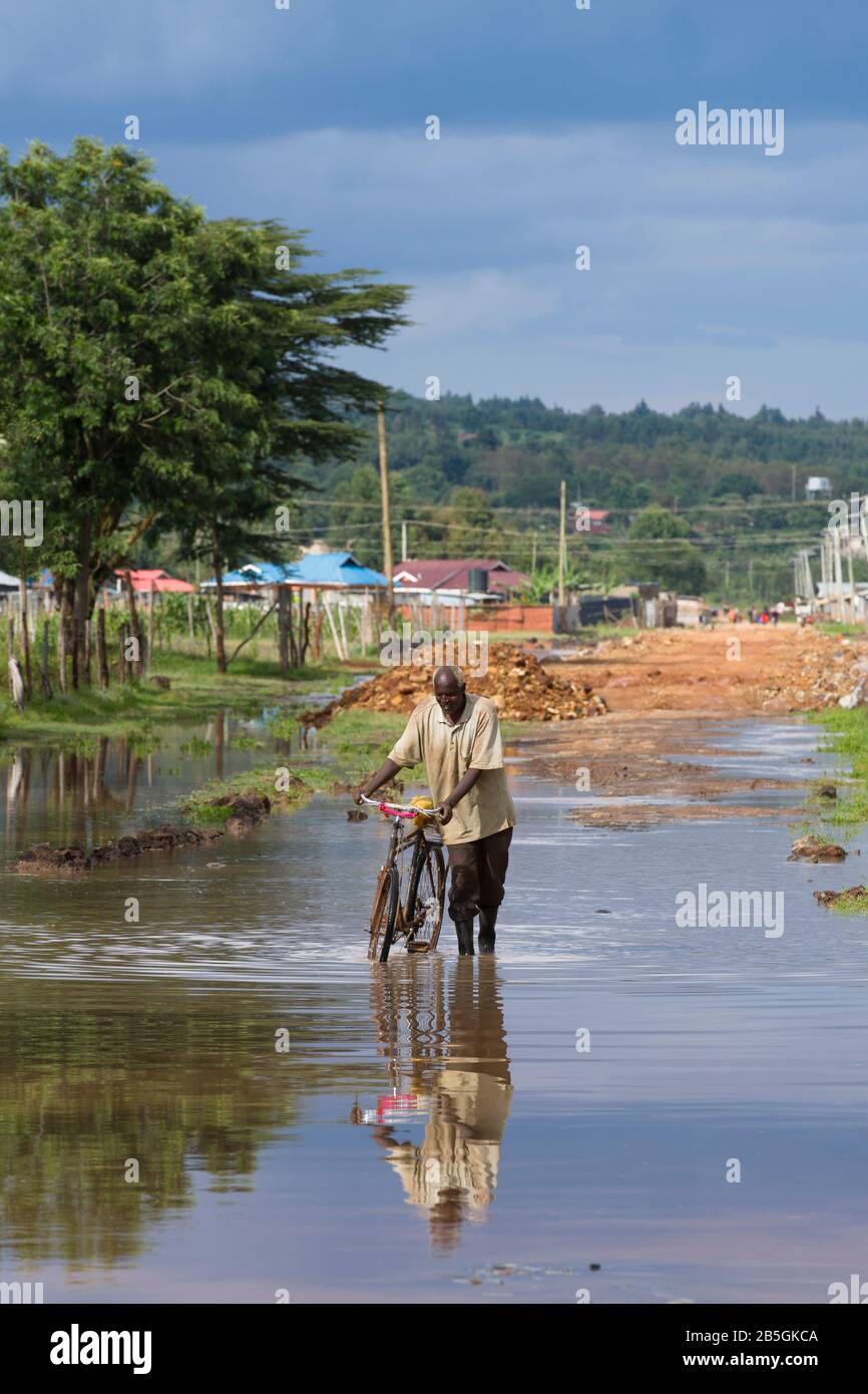 Man wading through flood water pushing a traditional roadster-style ...