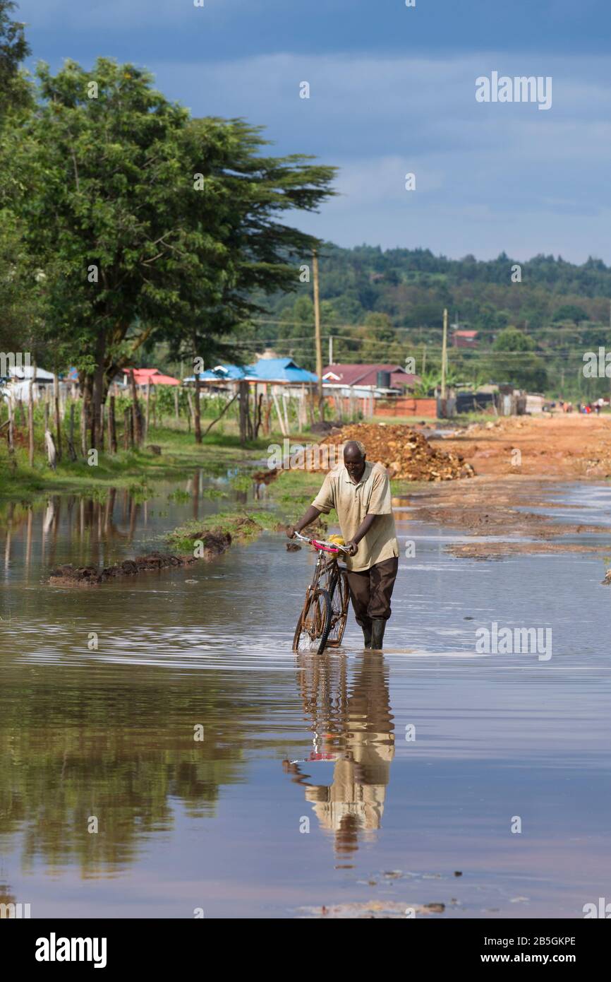 Man wading through flood water pushing a traditional roadster-style ...