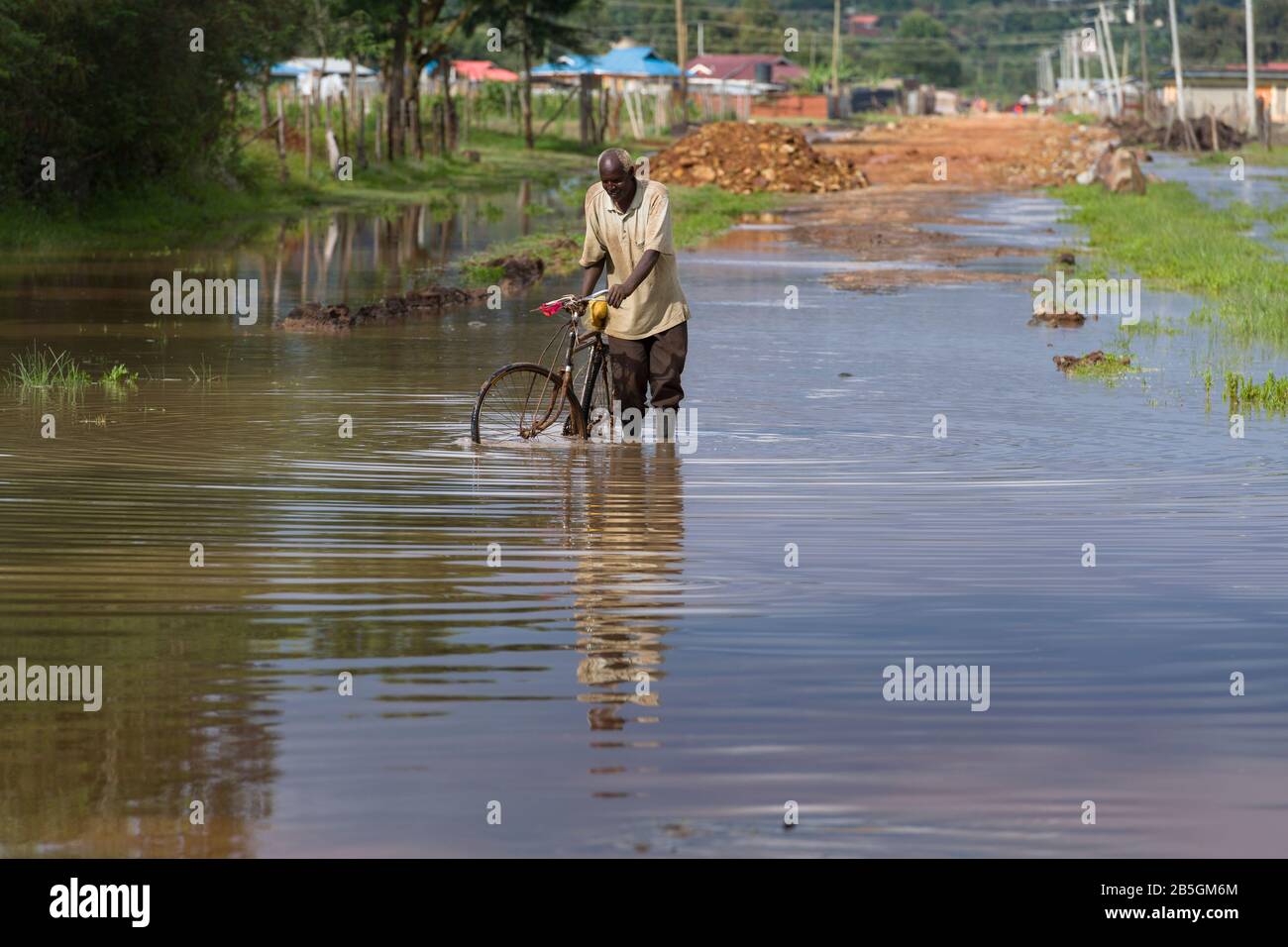 Man wading through flood water pushing a traditional roadster-style ...