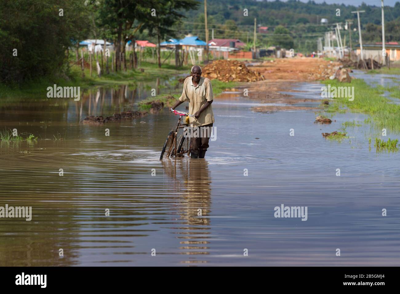 Man wading through flood water pushing a traditional roadster-style ...