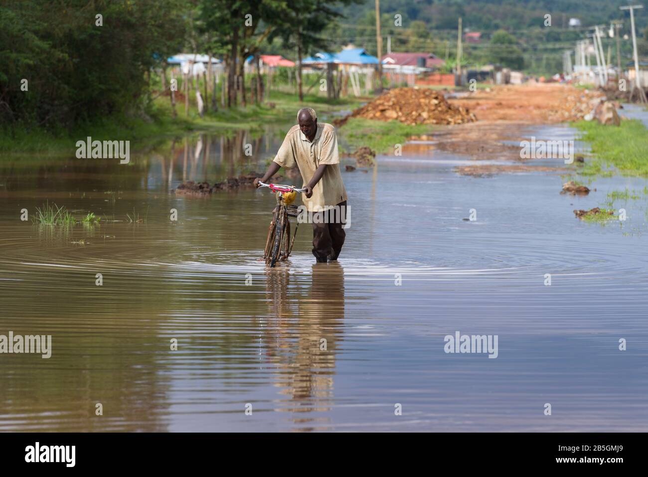 Man wading through flood water pushing a traditional roadster-style ...