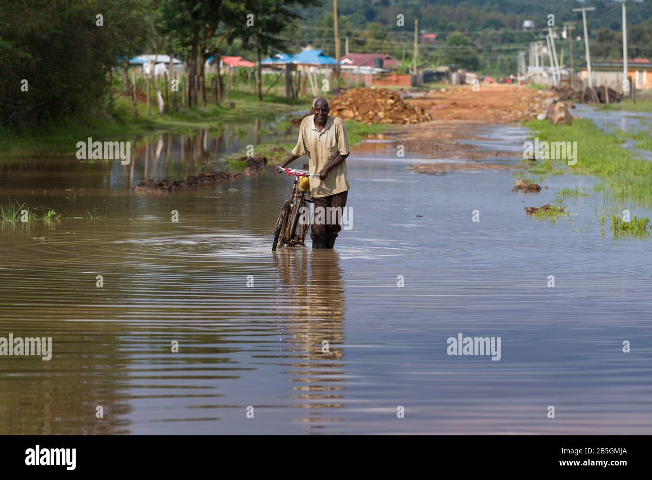 Man wading through flood water pushing a traditional roadster-style ...