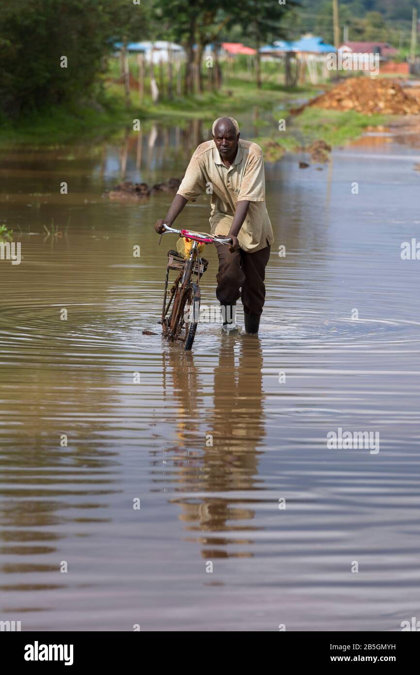 Man wading through flood water pushing a traditional roadster-style ...