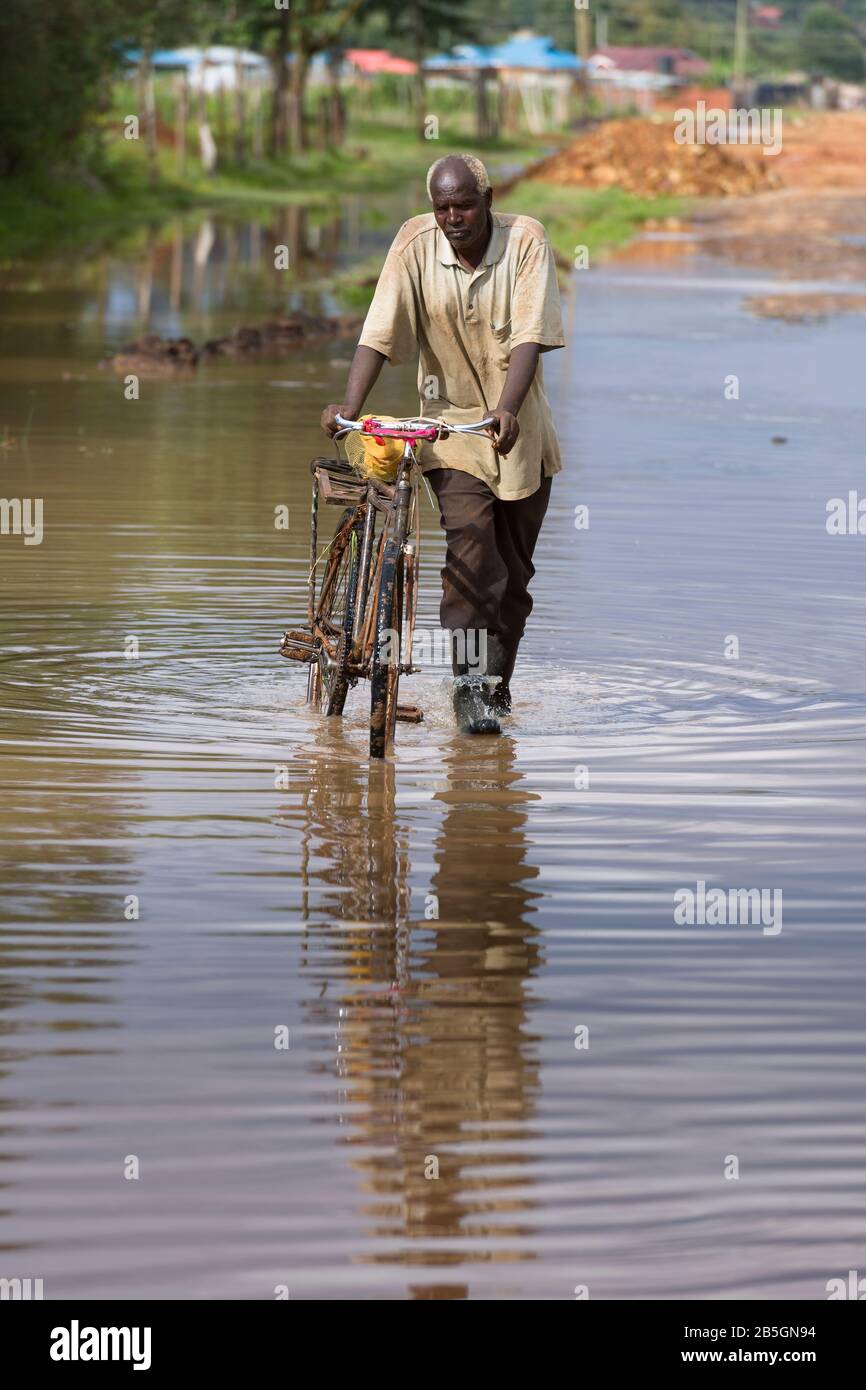Man wading through flood water pushing a traditional roadster-style ...
