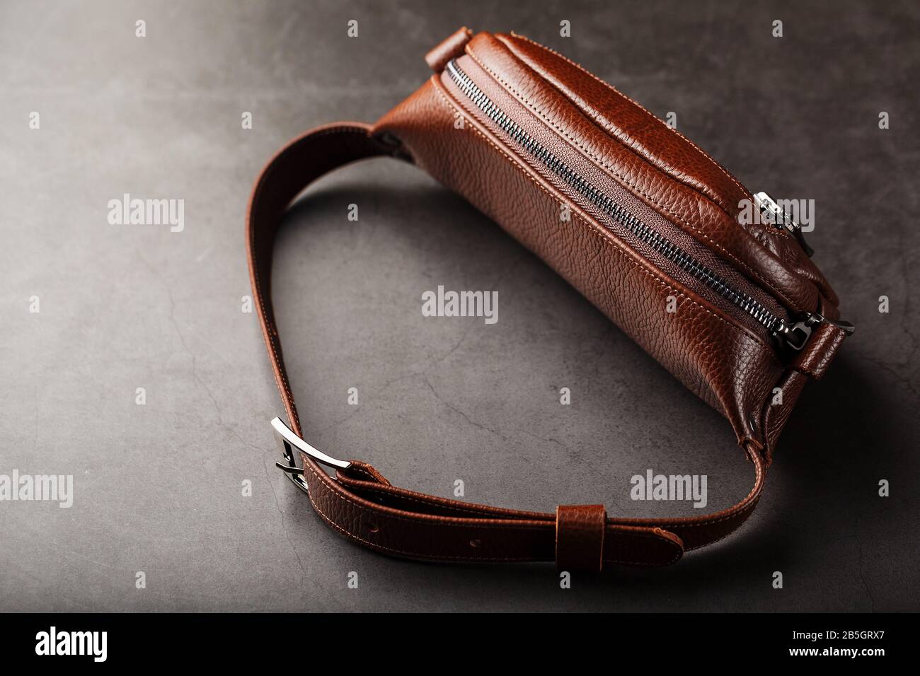A brown belt bag made of textured brown leather on a black stone ...