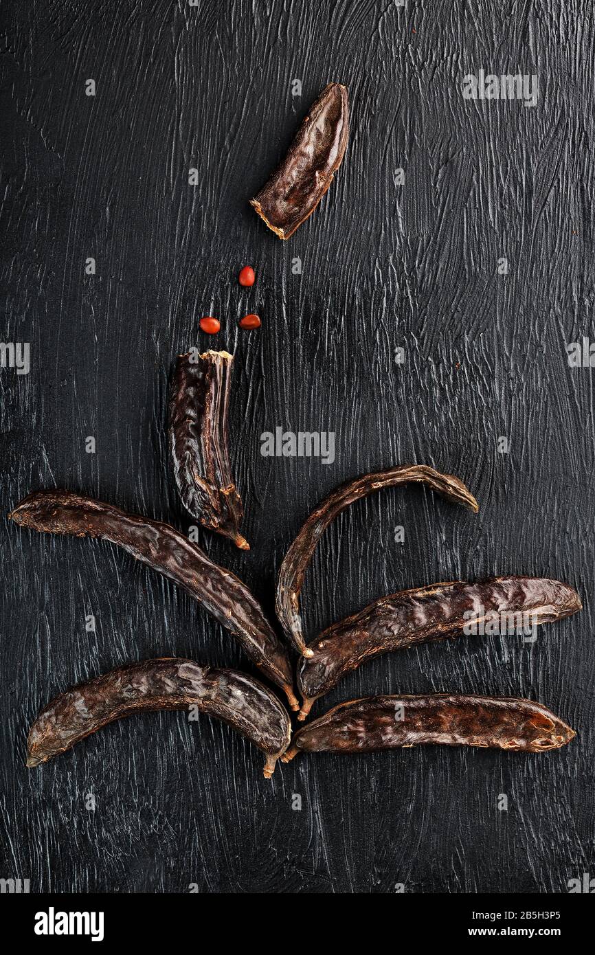 The fruit of the carob tree on black textured background in the form ...