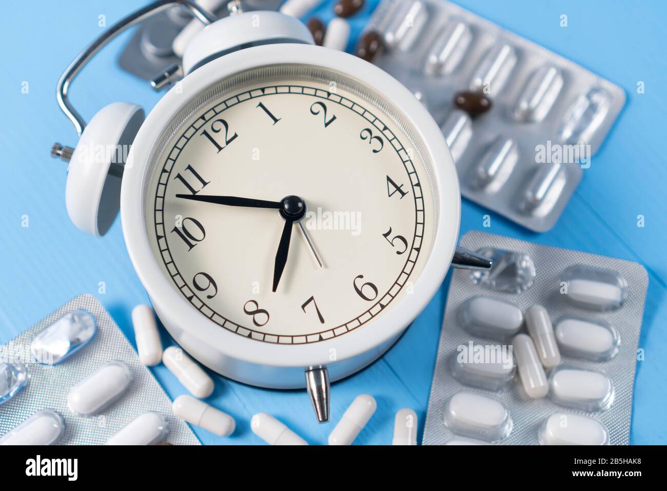 Pile of medical pills and capsules with an alarm clock with black ...