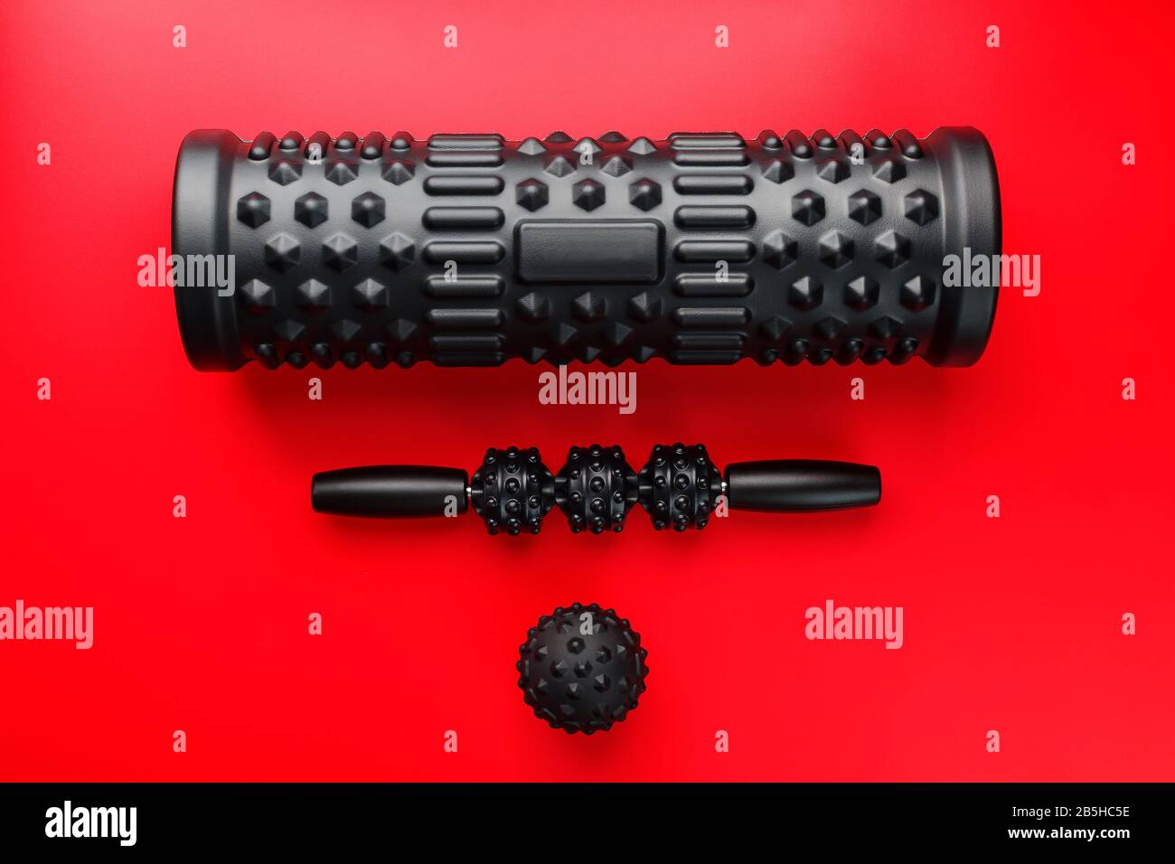 Set of Black lumpy foam massage roller, body roller, rubber ball on red ...