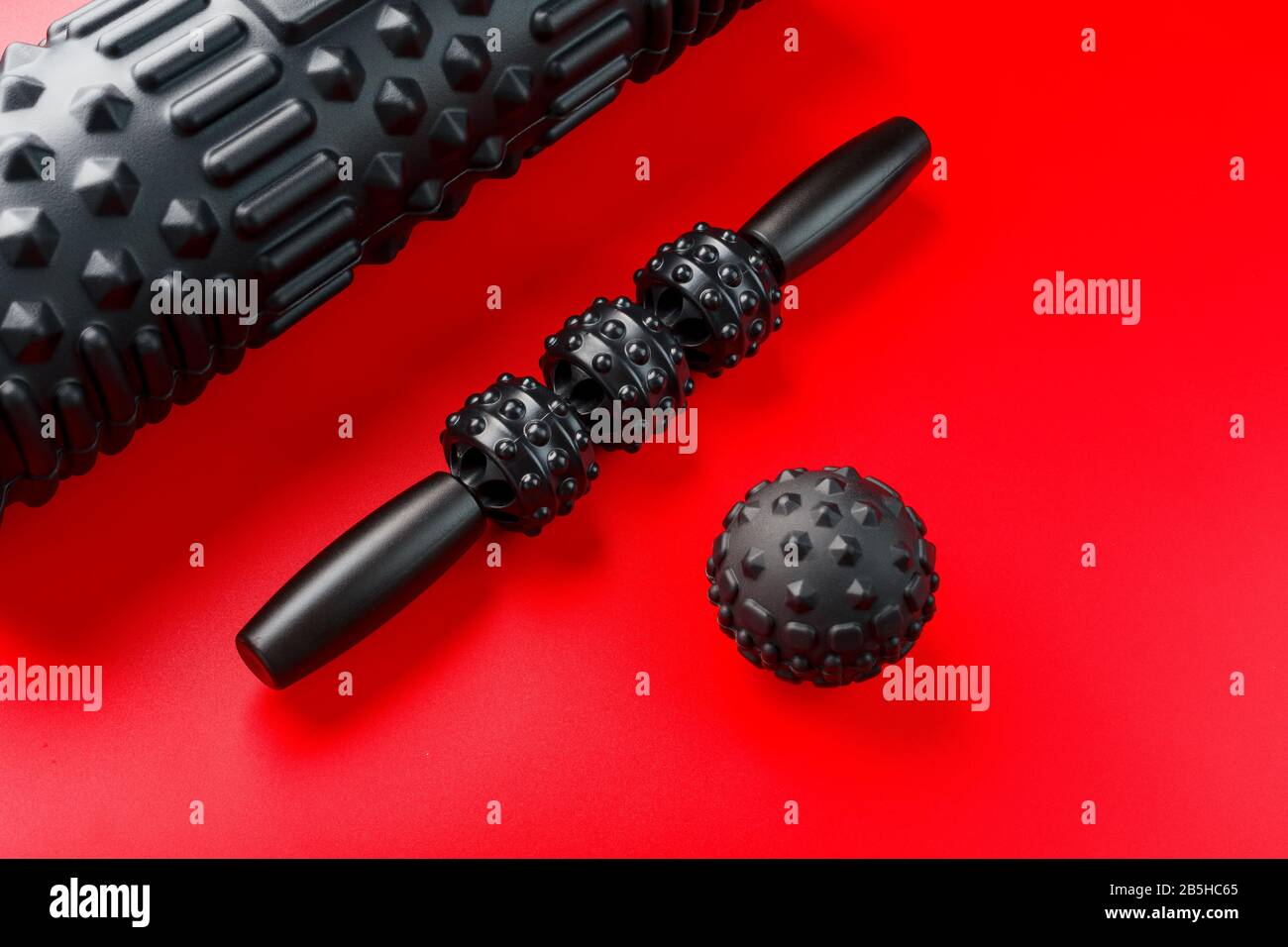 Set of Black lumpy foam massage roller, body roller, rubber ball on red ...