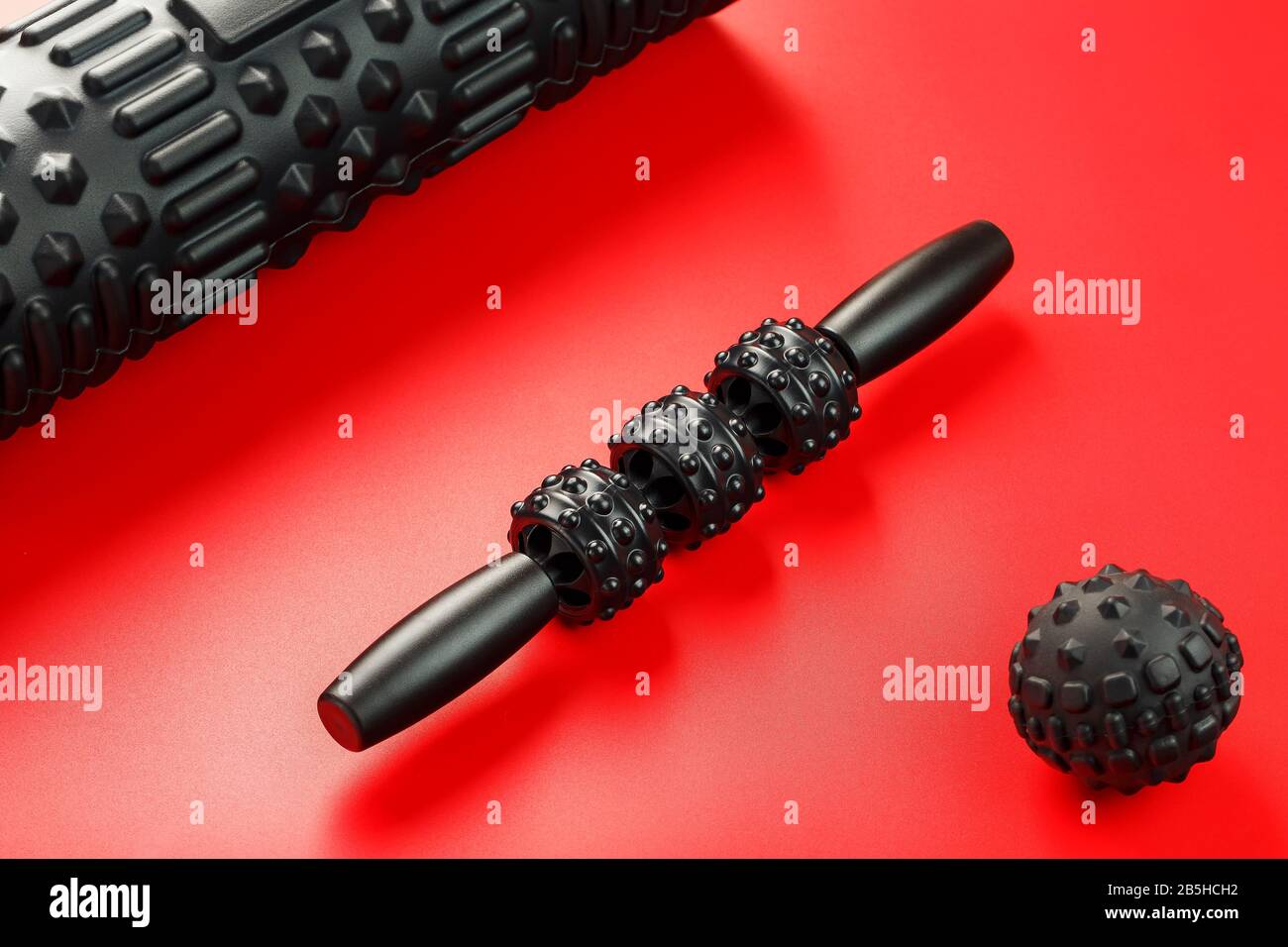Set of Black lumpy foam massage roller, body roller, rubber ball on red ...