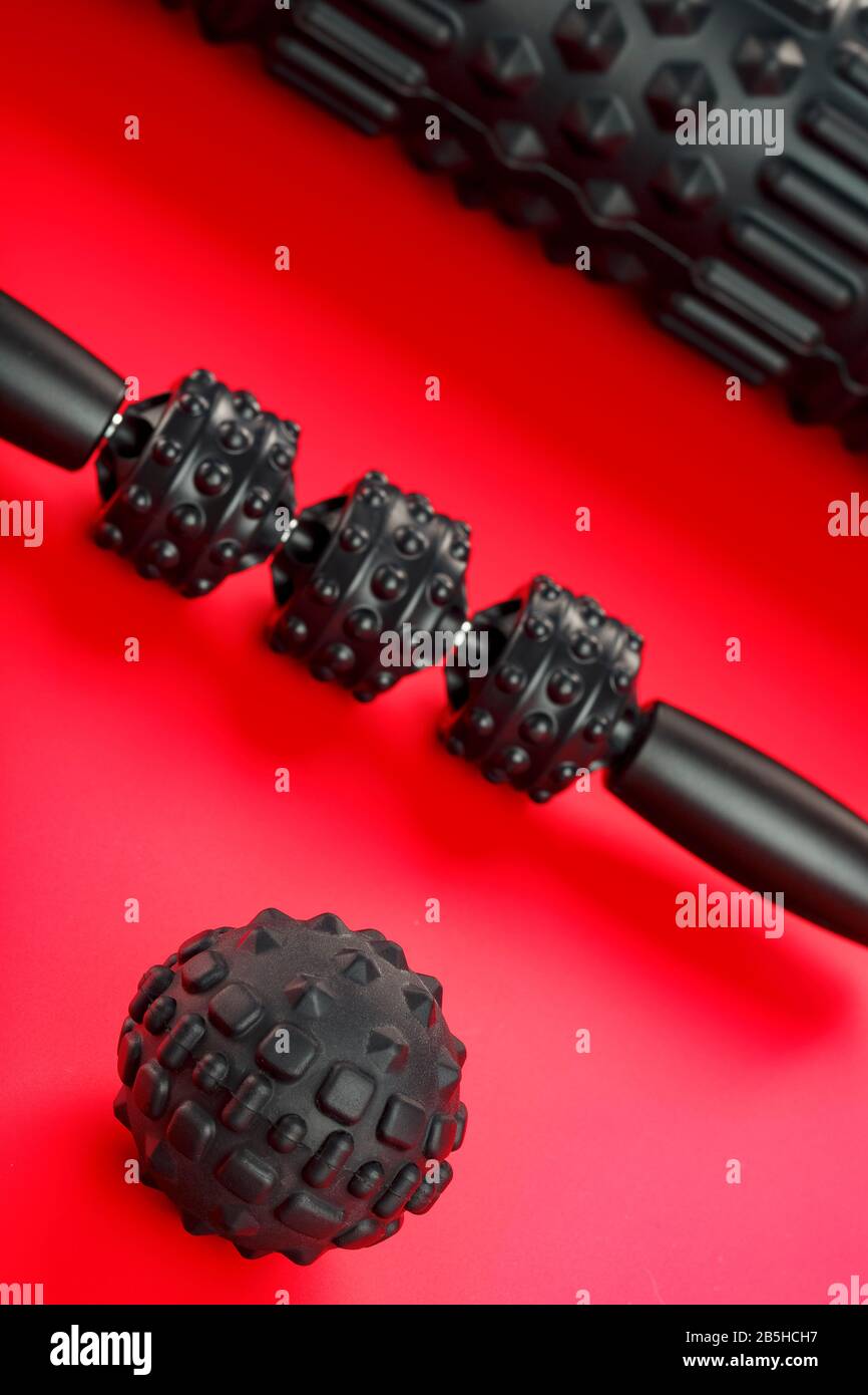 Set of Black lumpy foam massage roller, body roller, rubber ball on red ...