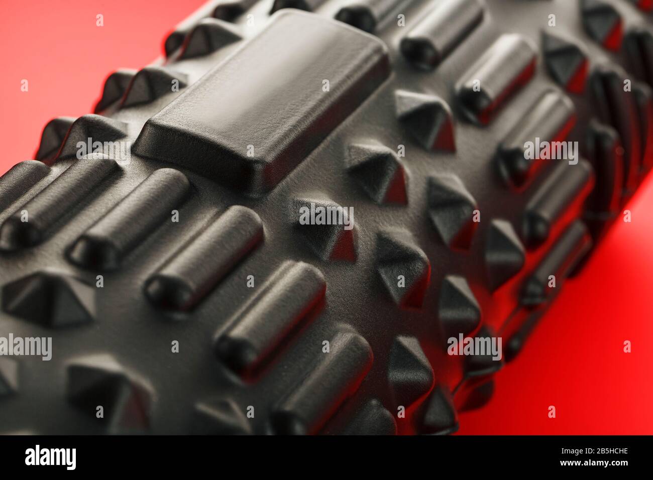Black lumpy foam massage roller on red background. For the mechanical ...