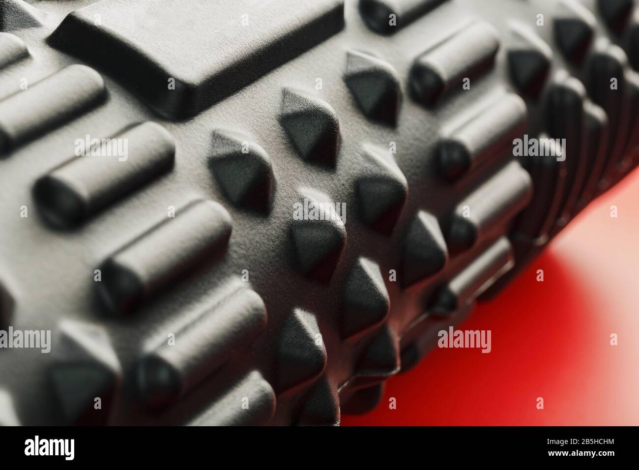 Black lumpy foam massage roller on red background. For the mechanical ...