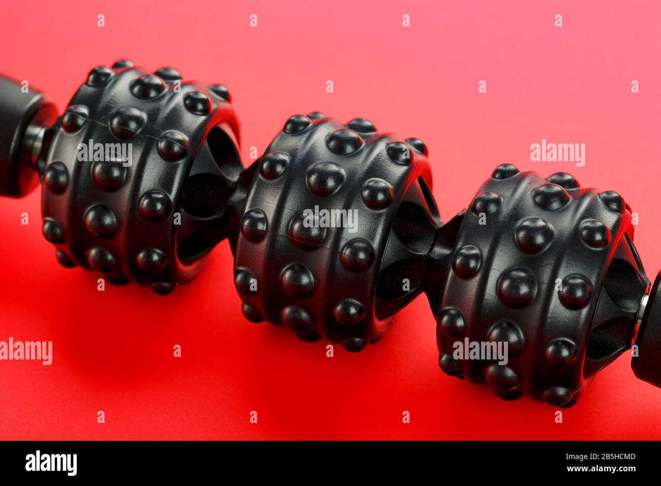 Black lumpy foam body massage roller on red background. For the ...