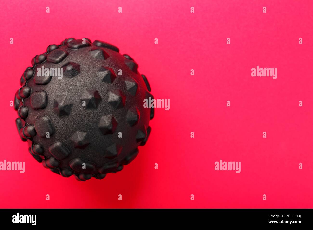 Black lumpy foam body massage ball on red background. For the ...