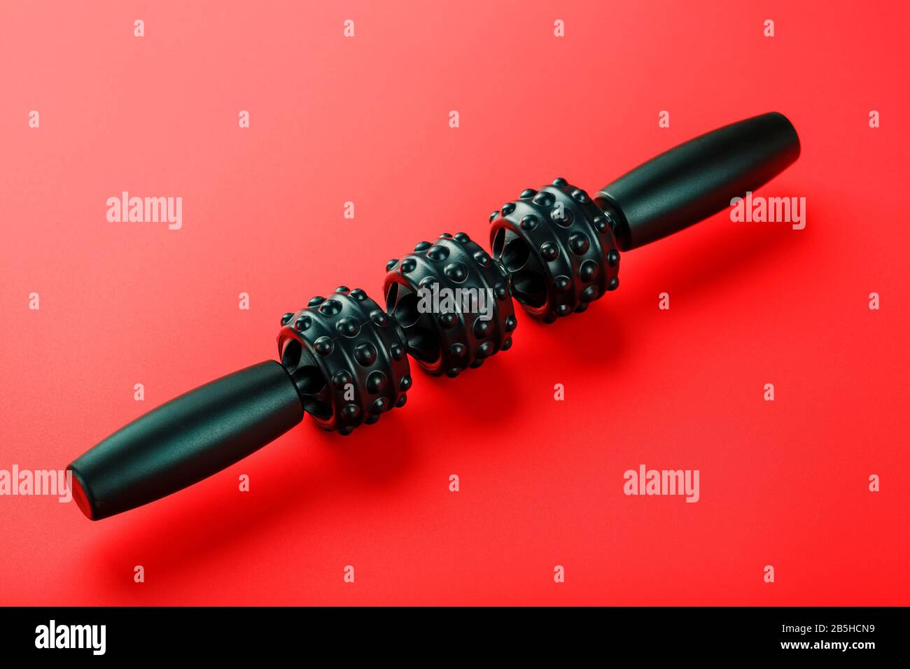 Black lumpy foam body massage roller on red background. For the ...
