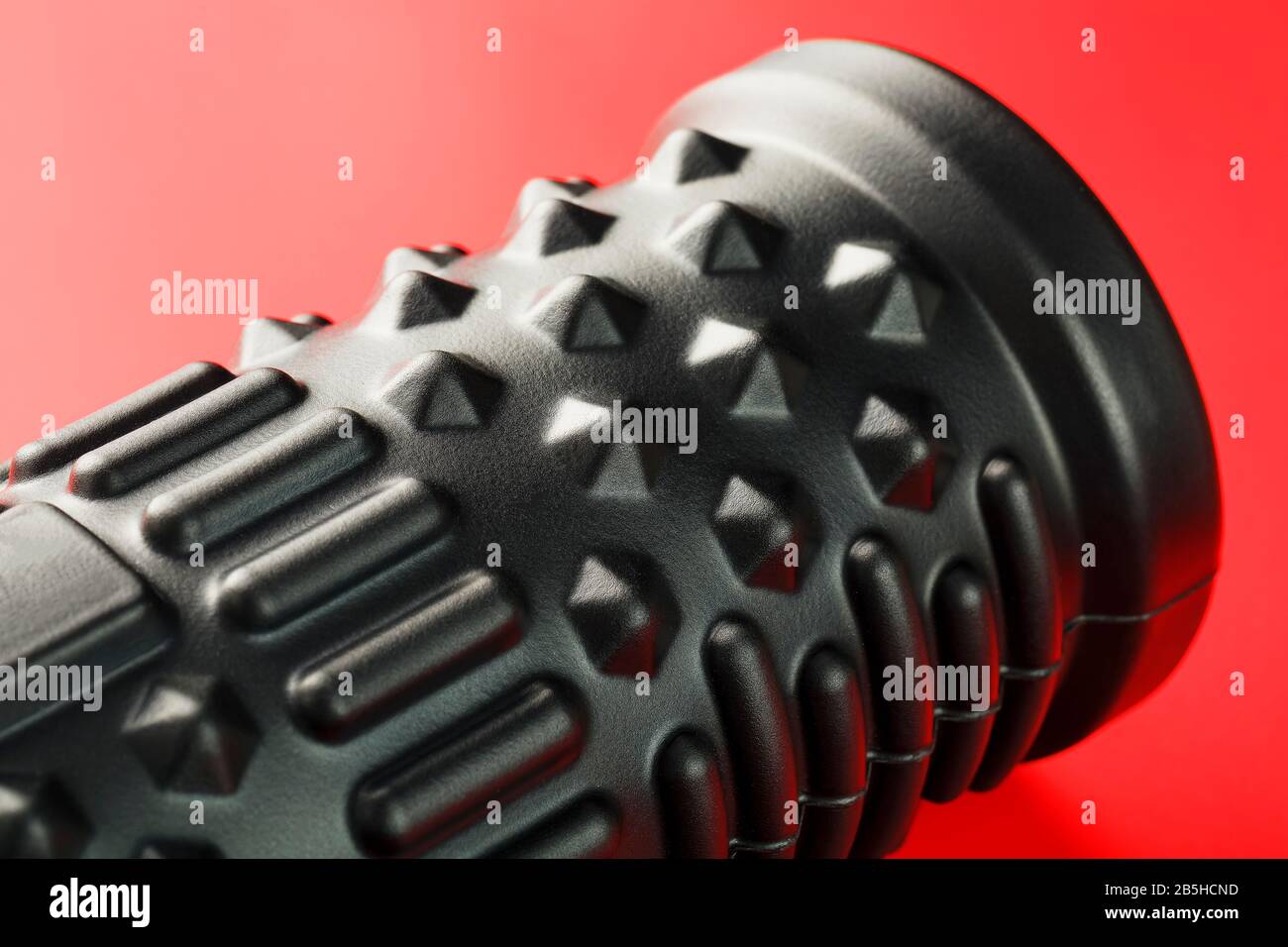 Black lumpy foam massage roller on red background. For the mechanical ...