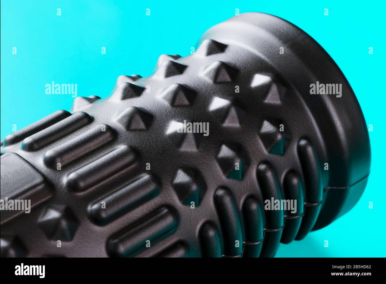 Black bumpy foam massage roller, body roller on blue background. For ...