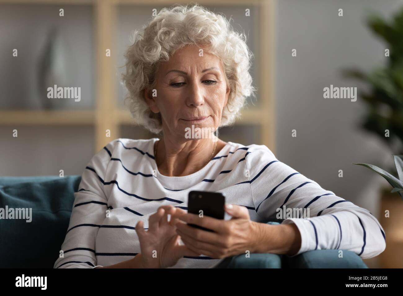 Modern elderly woman sit on couch texting on cell Stock Photo - Alamy