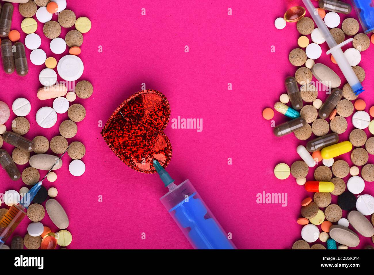 Many scattered colorful pills on pink background. Drugs, syringe and ...