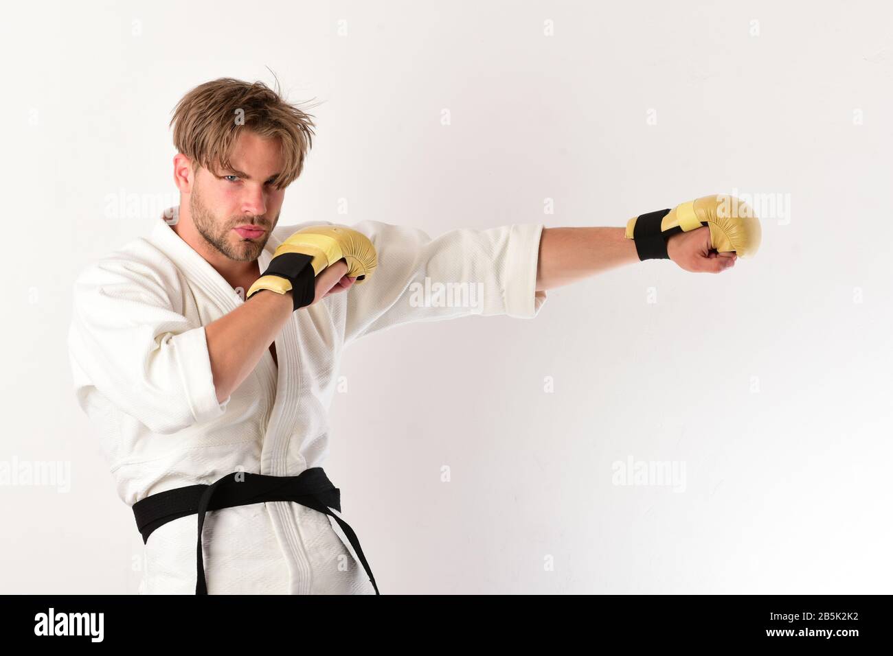 Guy poses in white kimono wearing golden boxing gloves. MMA fighter ...