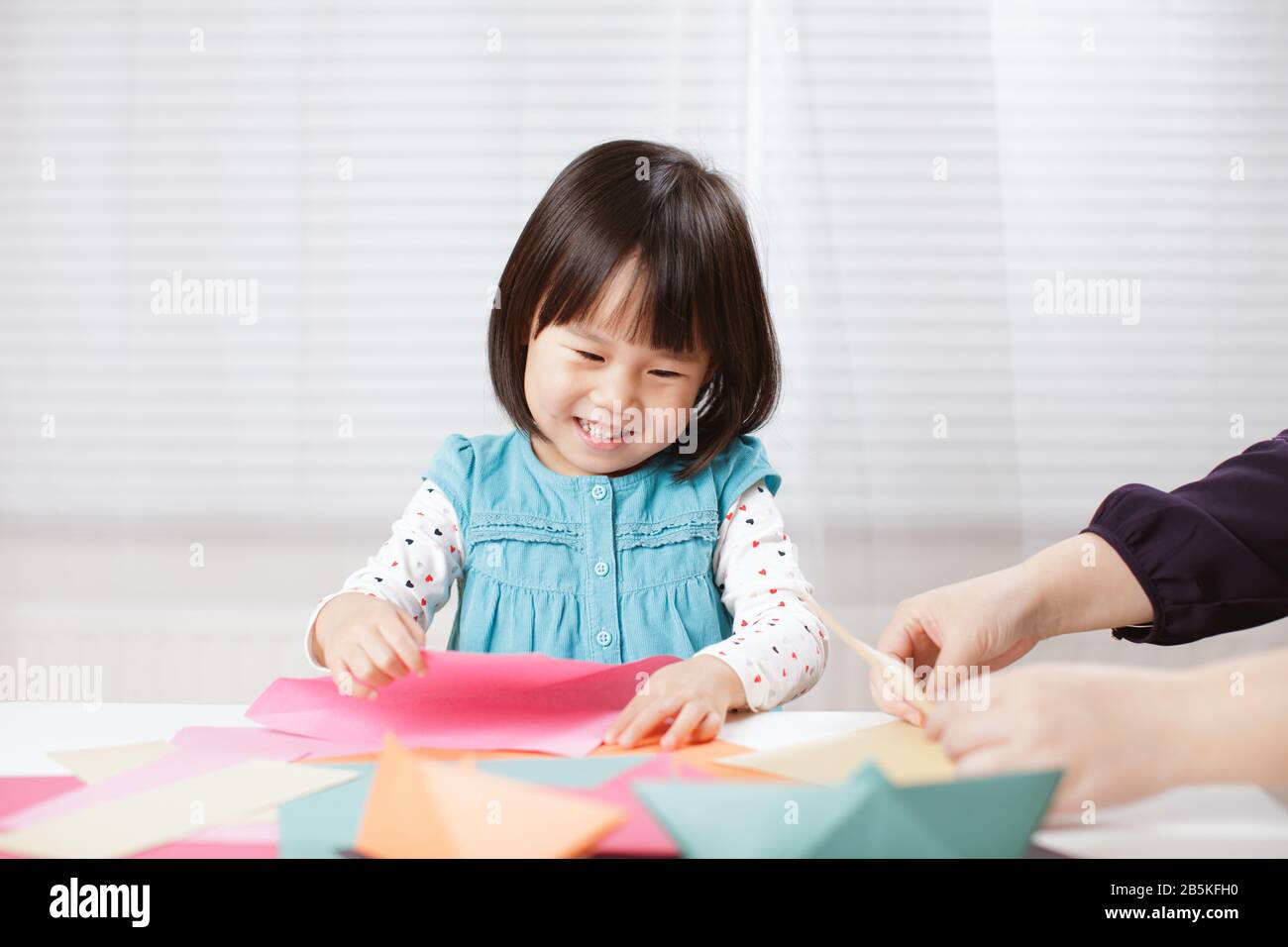 toddler girl learn making Origami at home against white background ...